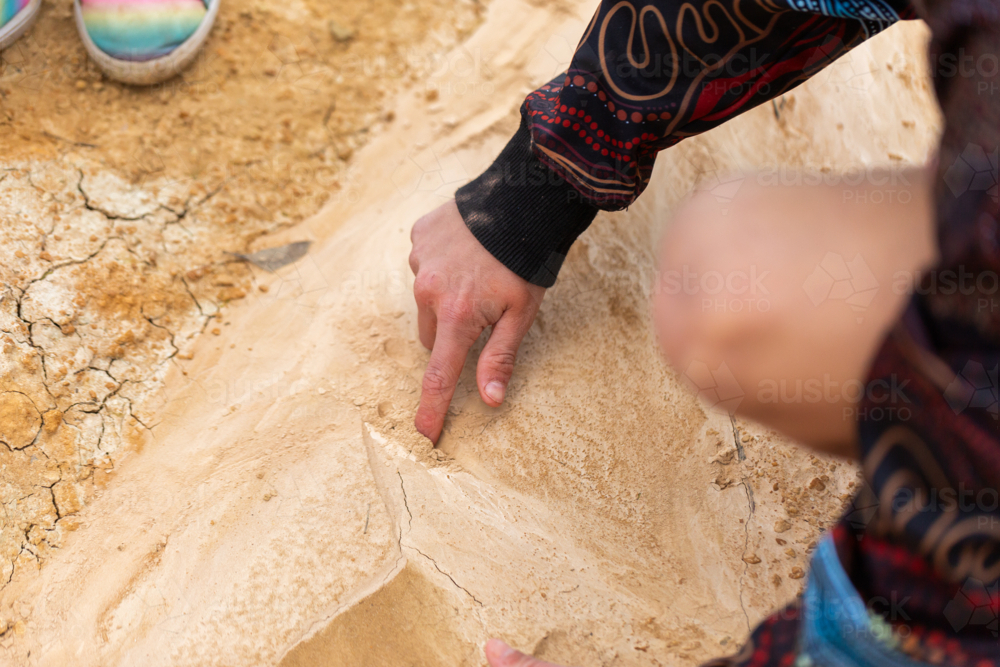Image of Aboriginal boy writing with fingers in soft dirt - Austockphoto