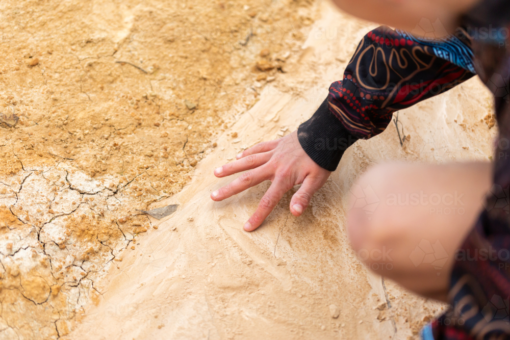 Image of Aboriginal boy writing with fingers in soft dirt - Austockphoto