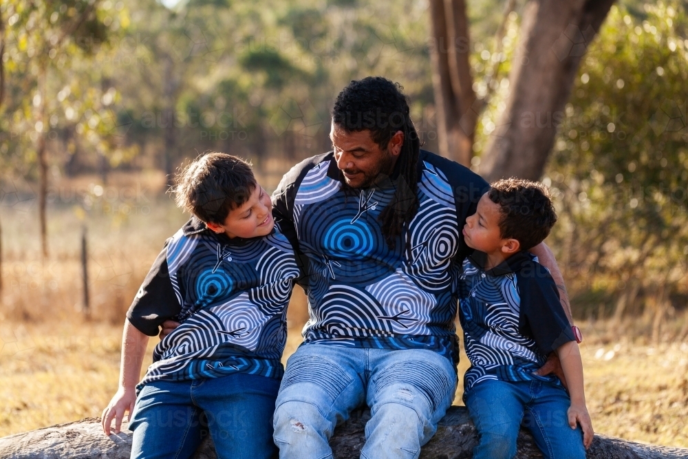 Image of Aboriginal dad sitting together with sons on log in bush ...