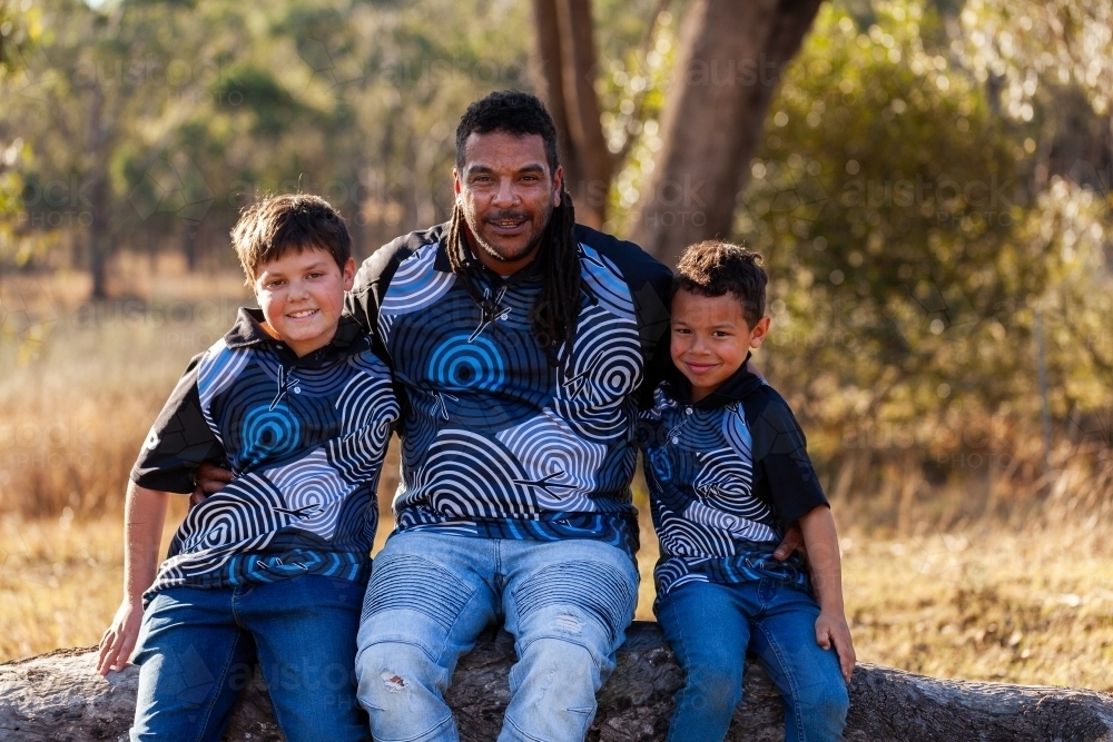 Image of Aboriginal dad sitting together with sons on log in bush ...