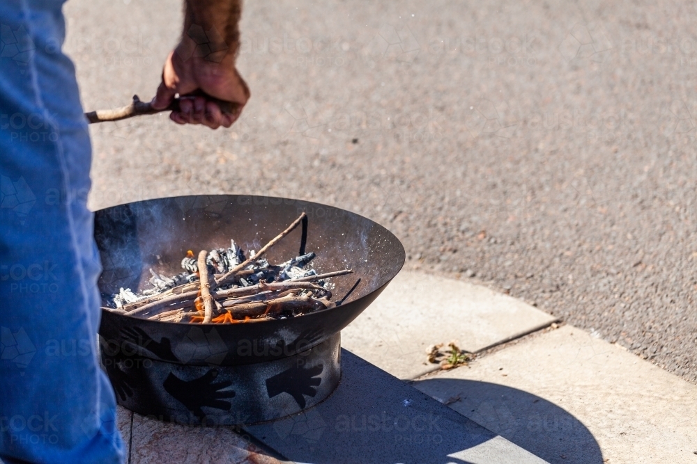 Image of Aboriginal elder putting sticks in fire pit for smoking ...