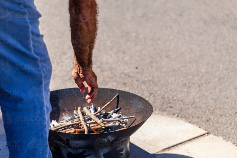 Image of Aboriginal elder putting sticks in fire pit for smoking ...