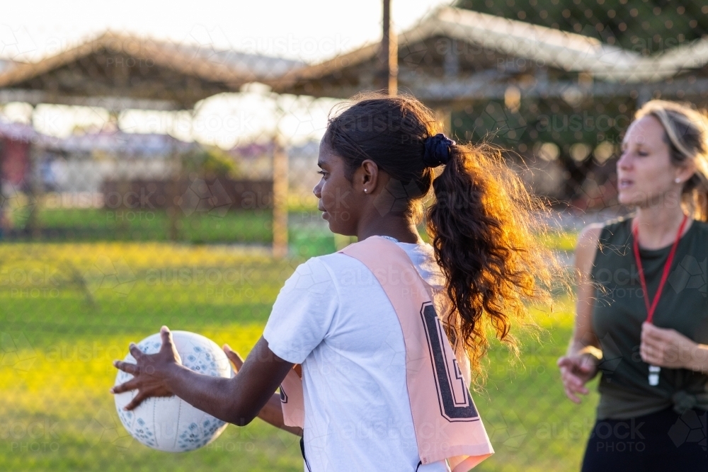Image of aboriginal girl catching netball with Caucasian umpire or ...