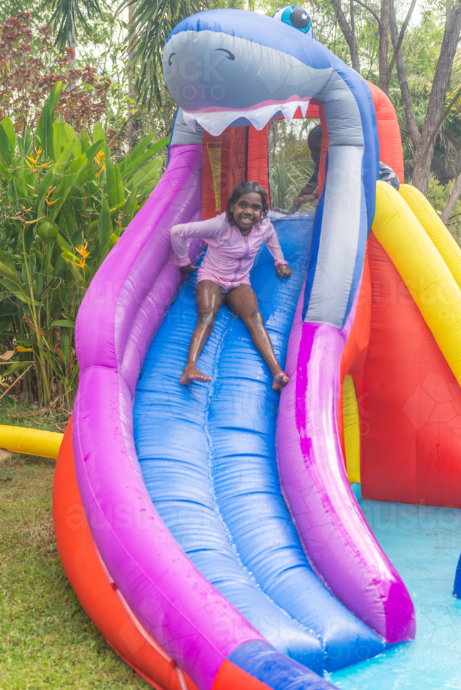 Image of Aboriginal girl on water slide at home - Austockphoto