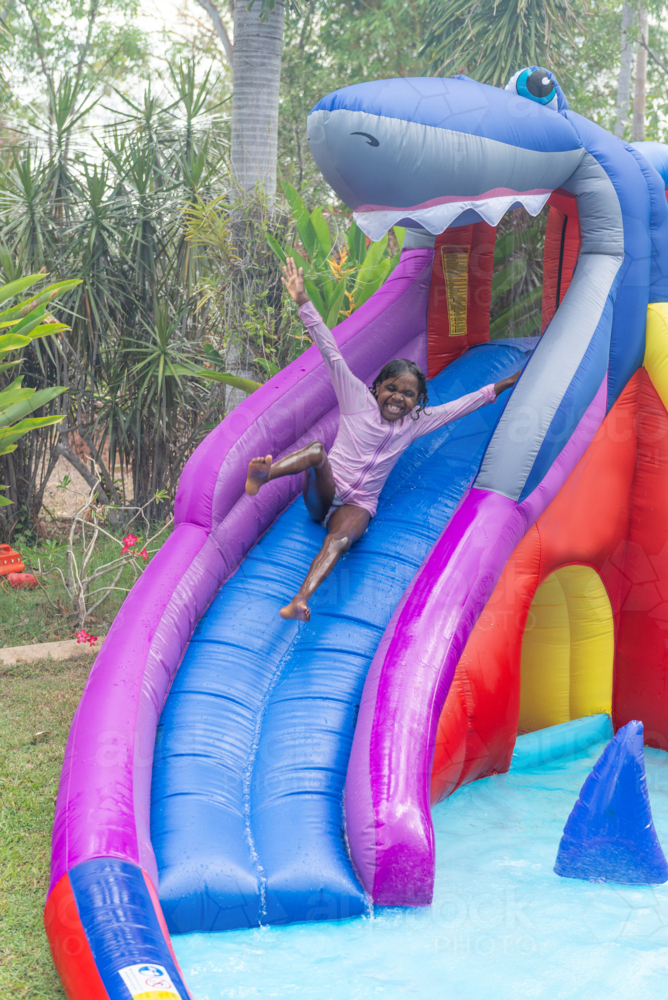Image of Aboriginal girl on water slide at home - Austockphoto