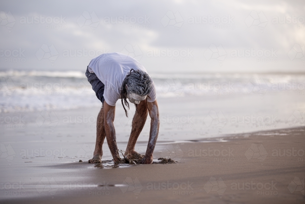 Image of Aboriginal man digging with his hands on a beach - Austockphoto