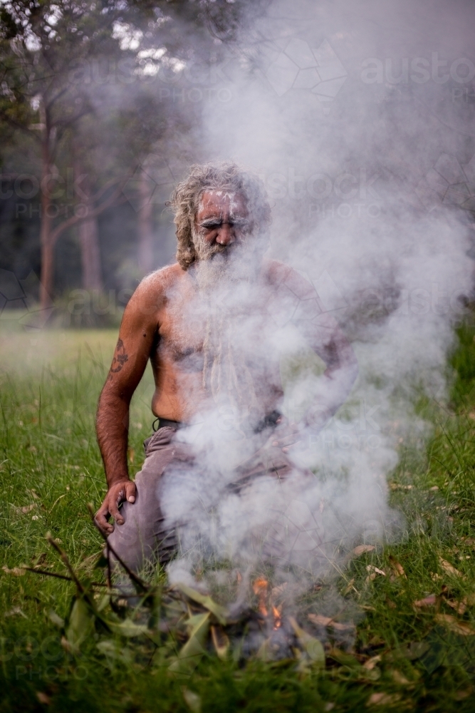 Image of Aboriginal man kneeling behind smoke at a smoking ceremony ...