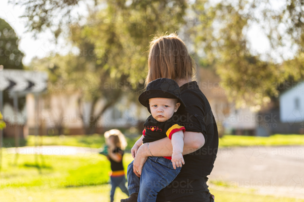 Image of Aboriginal mum holding baby boy in arms while watching toddler ...