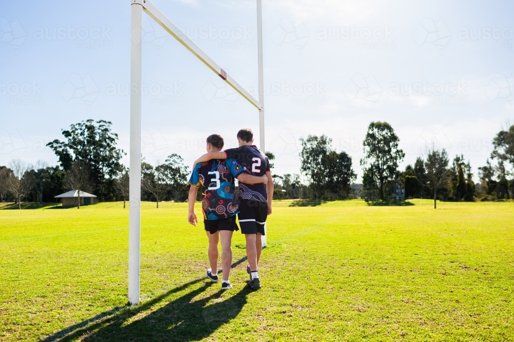 Image of Aboriginal teammates walking towards goal post on footy field ...