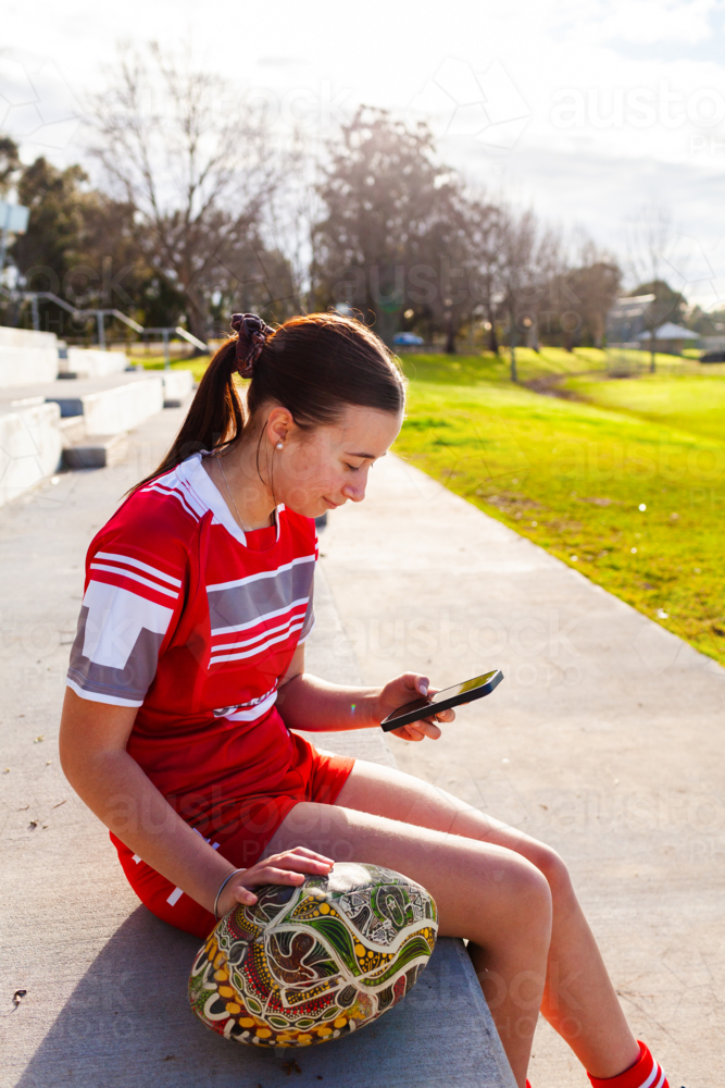 Image of Aboriginal teenager footy player sitting using phone beside ...