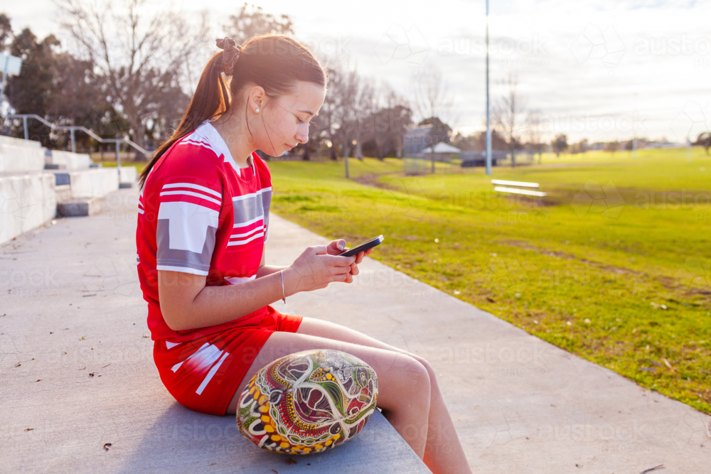 Image of Aboriginal teenager footy player sitting using phone beside ...
