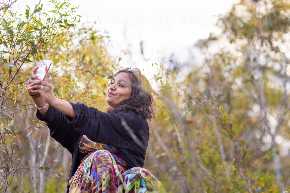 Image of aboriginal woman in the bush holding phone up to take a selfie ...