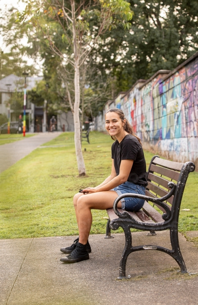 Image of Aboriginal woman sitting on a bench in an urban park smiling ...