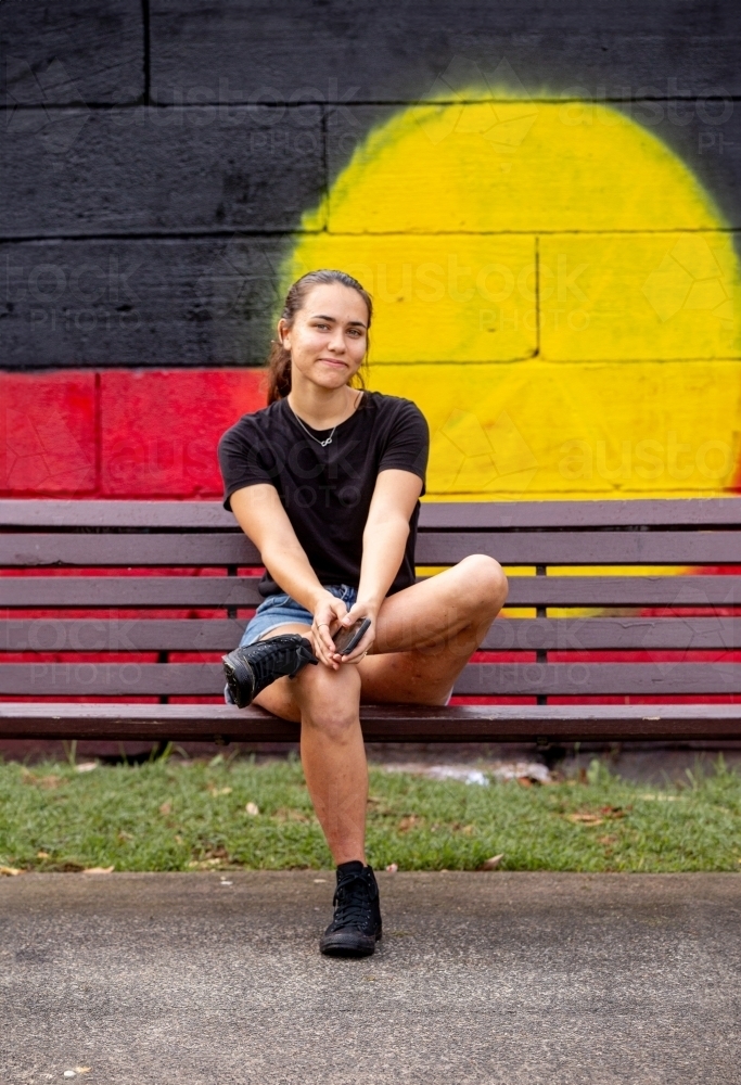 Image of Aboriginal woman sitting on a park bench in front of a mural ...