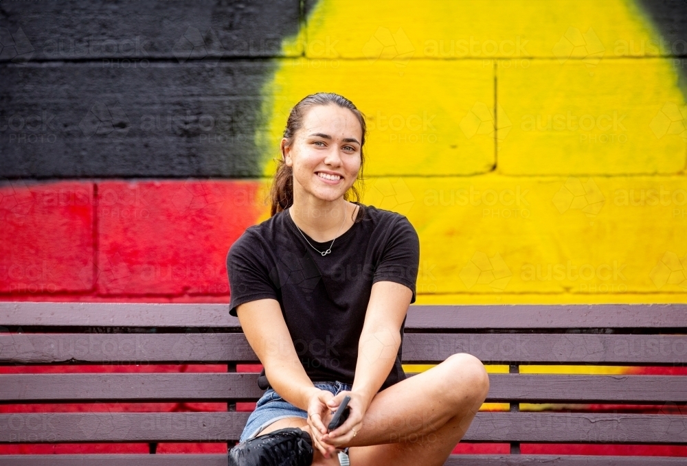 Image of Aboriginal woman sitting on a park bench in front of a mural ...