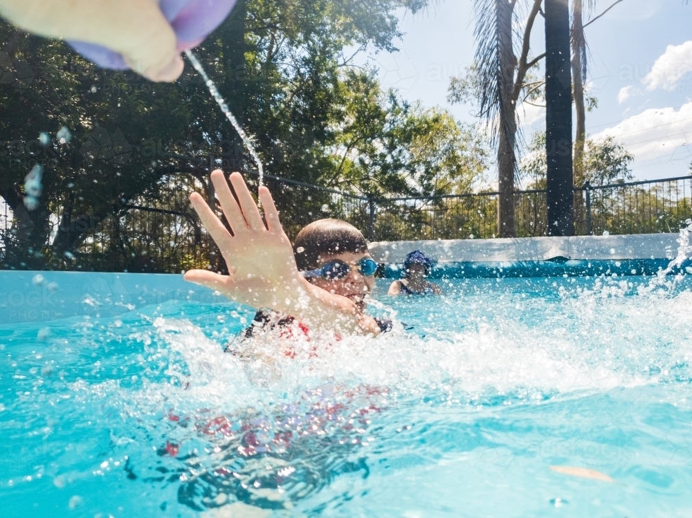 Image of Action shot of sibling squirting water fight in pool - cooling ...
