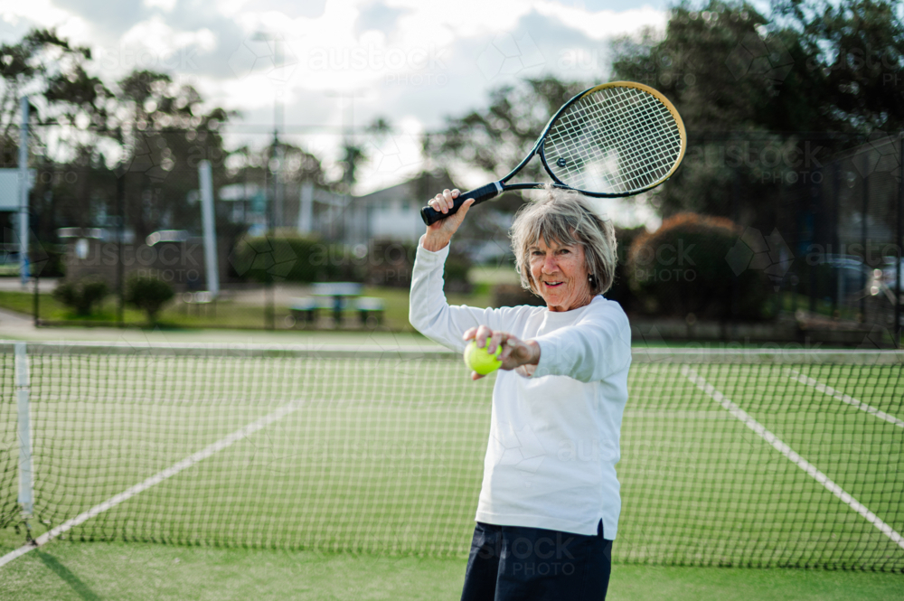 Image of Active older woman preparing to hit a tennis ball outdoors ...
