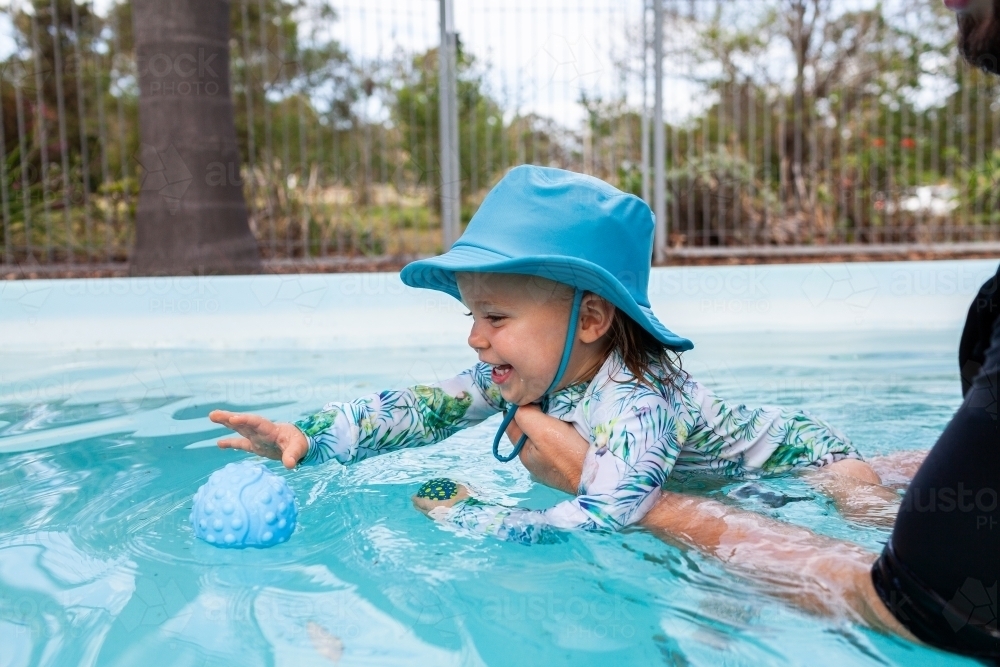 Image of Adult holding toddler kid in backyard swimming pool practicing ...