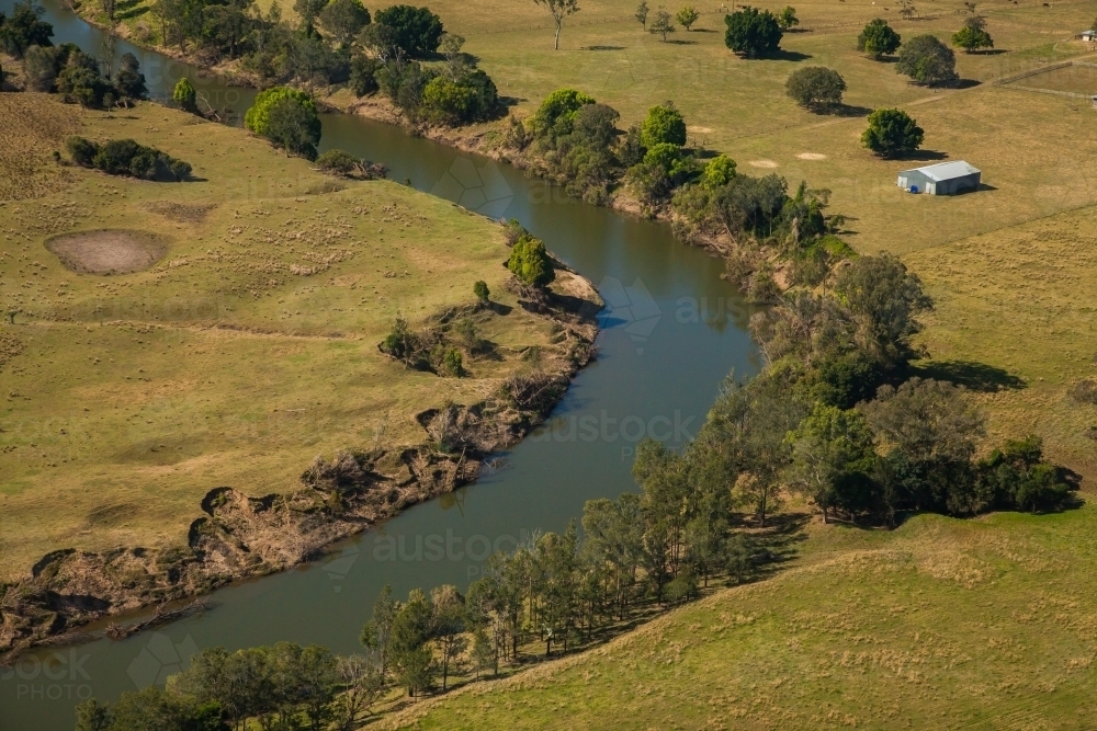 Image of Aerial of tree lined river bend beside farms - Austockphoto