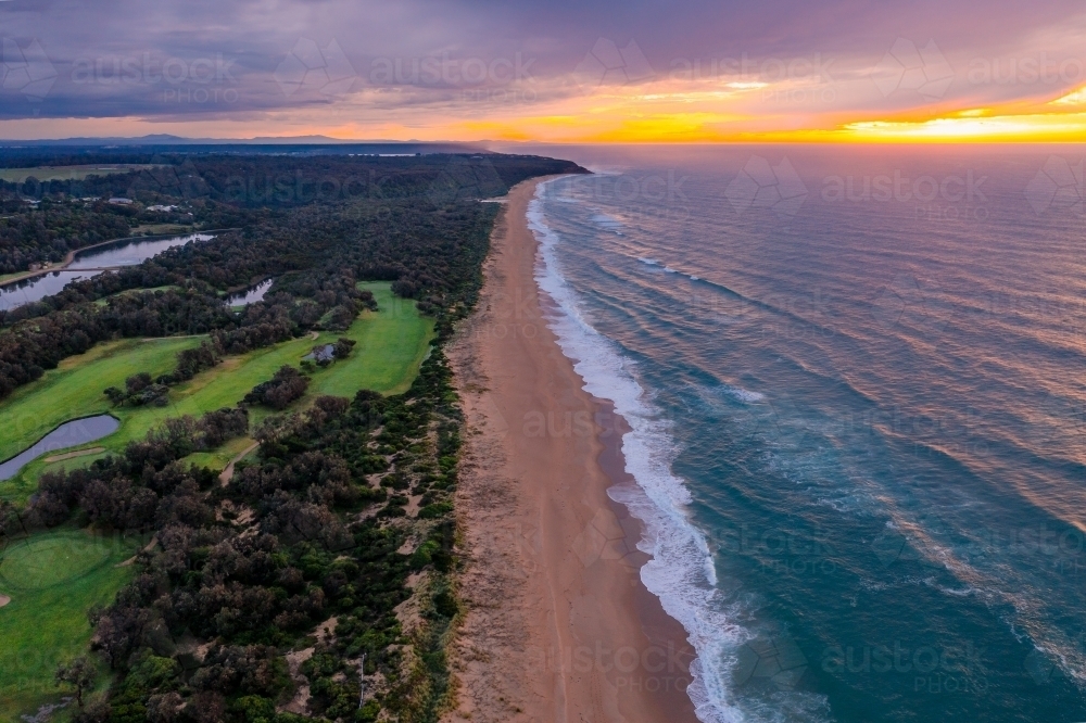 Image of Aerial view down a long sandy beach alongside a golf course ...