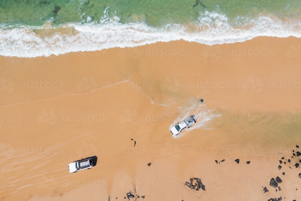 Image of Aerial view of 4WDs driving through water on a sandy beach ...