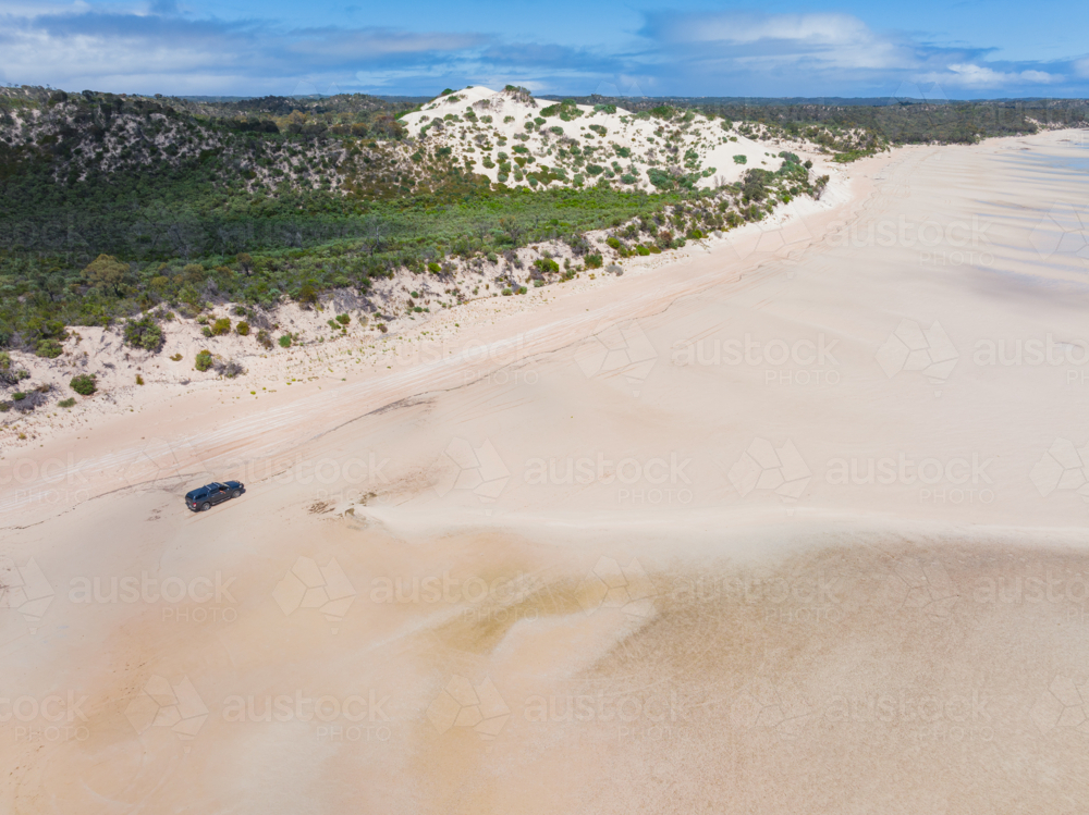 Image of Aerial view of a 4wd driving above the tide line on a wide ...