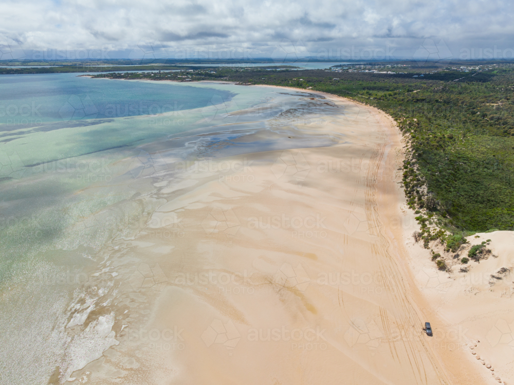 Image of Aerial view of a 4wd driving above the tide line on a wide ...