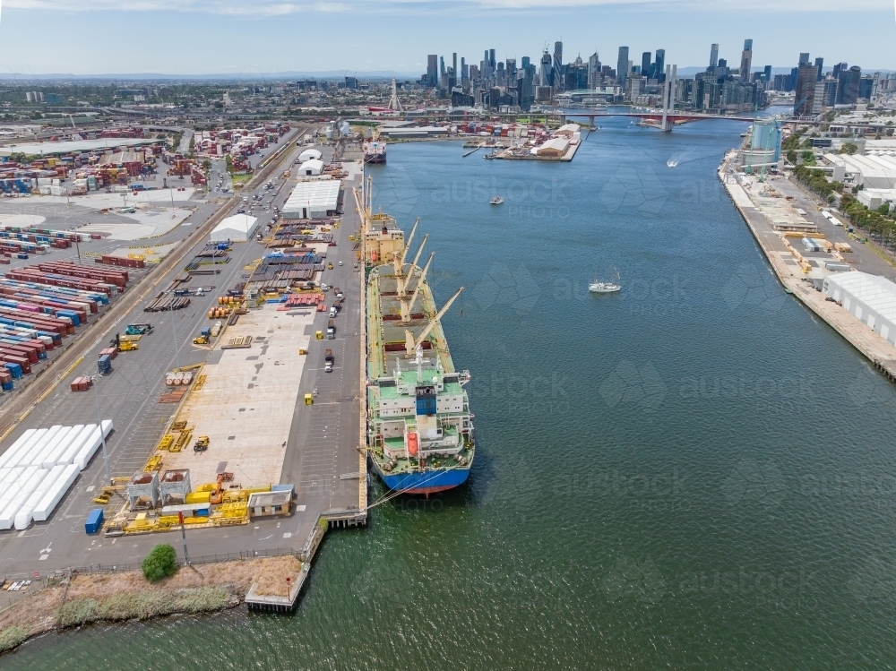 Image of Aerial view of a cargo ship at a river port and a city skyline ...