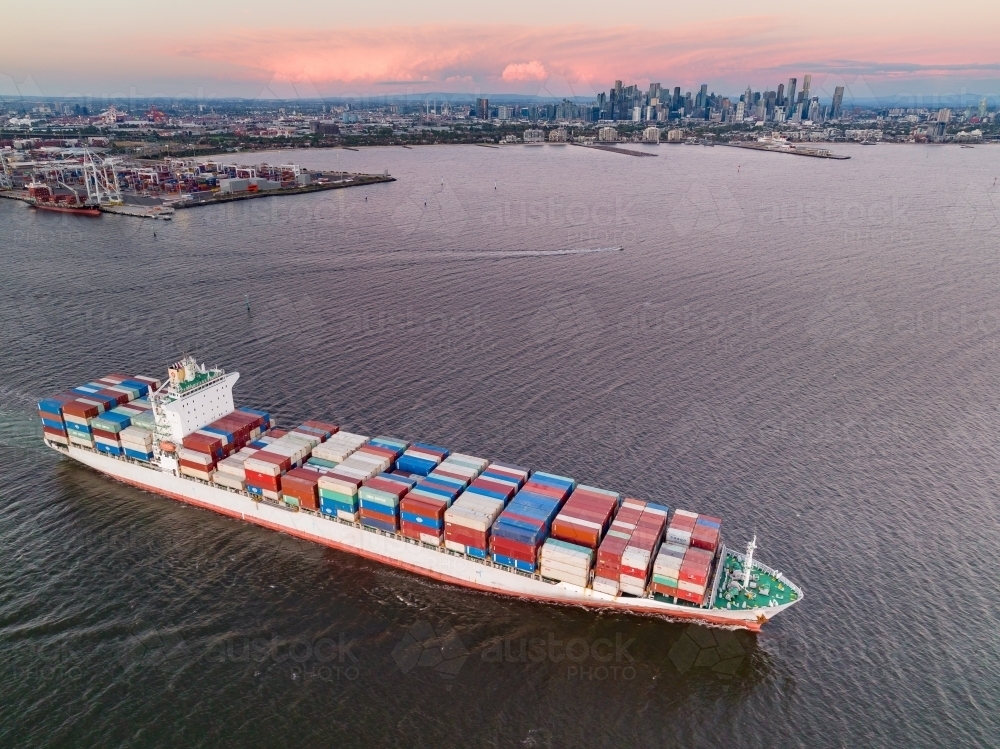 Image of Aerial view of a cargo ship leaving port at sunset, fully ...