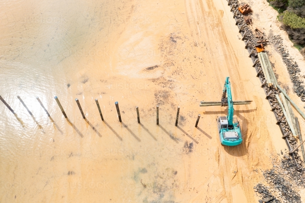 Image of Aerial view of a colourful digger carrying poles along a sandy ...