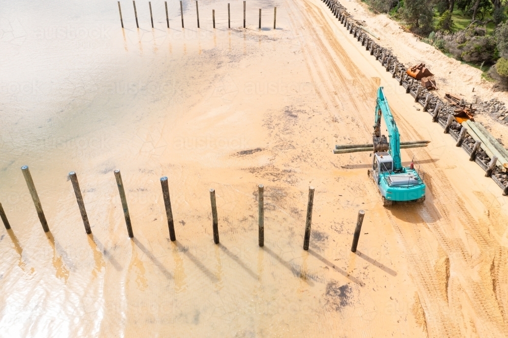 Image of Aerial view of a colourful digger carrying poles along a sandy ...