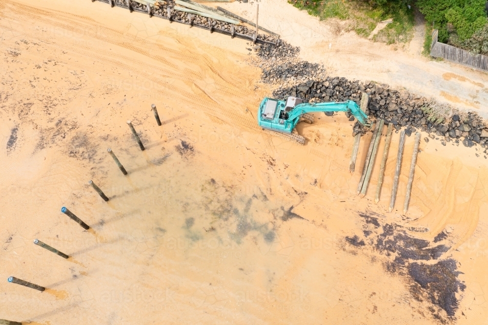 Image of Aerial view of a colourful digger carrying poles along a sandy ...