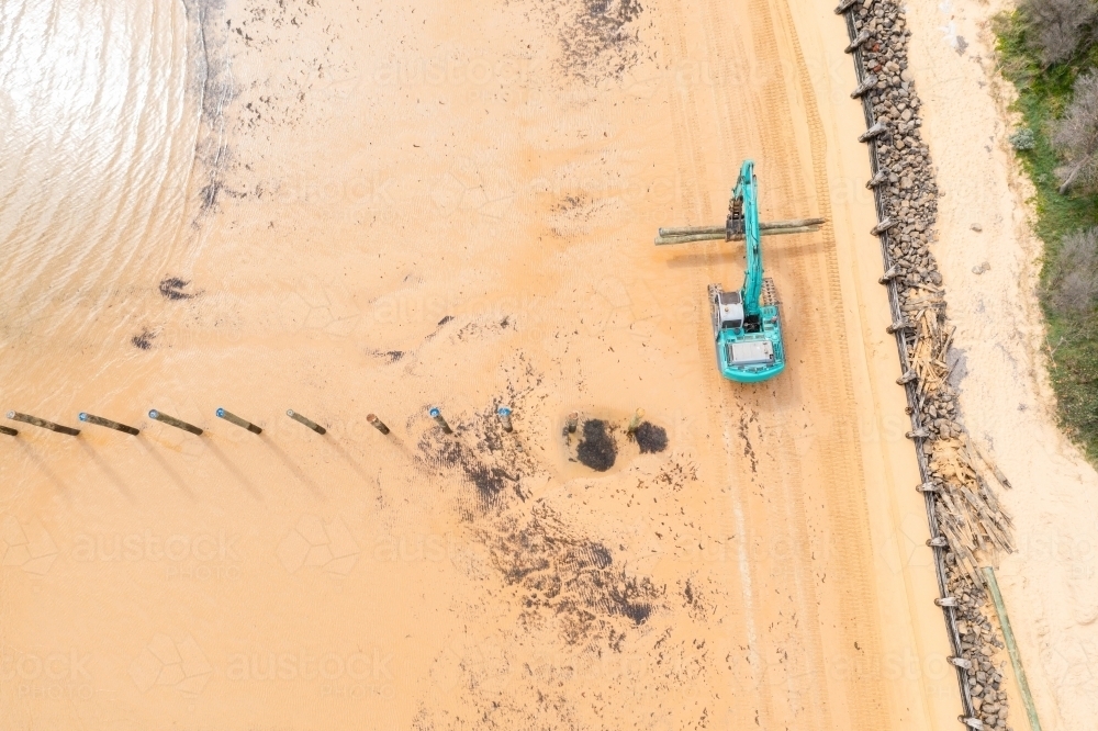 Image of Aerial view of a colourful digger carrying poles along a sandy ...