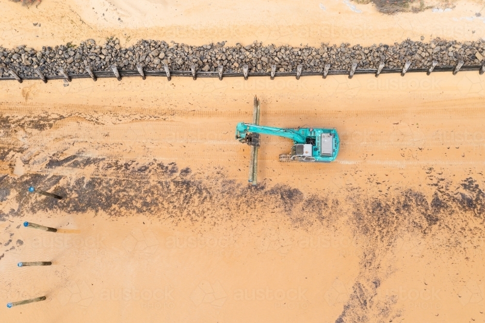 Image of Aerial view of a colourful digger carrying poles along a sandy ...