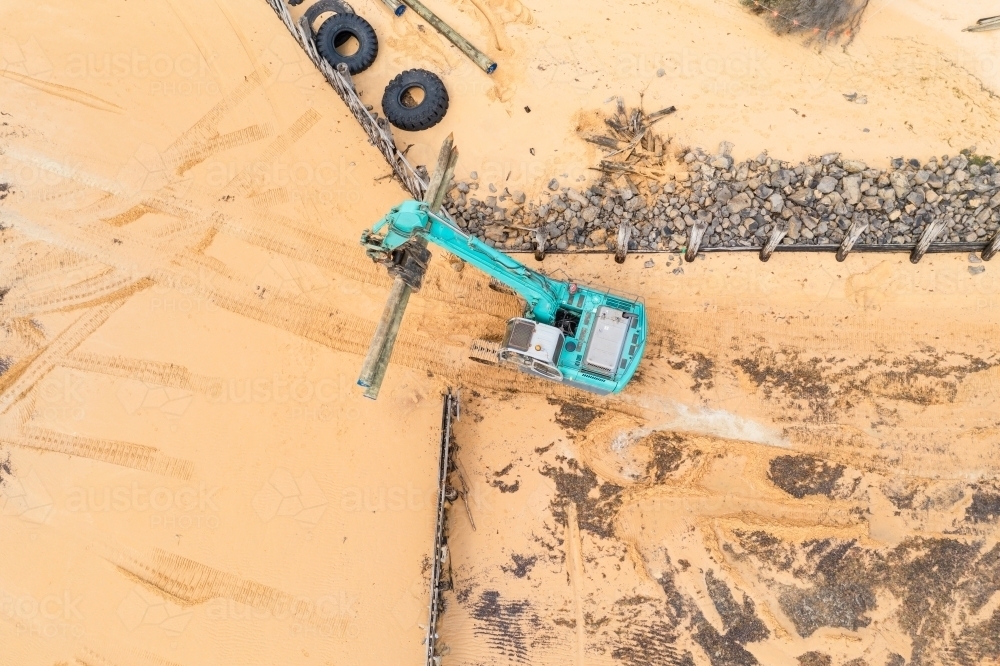 Image of Aerial view of a colourful digger carrying poles along a sandy ...
