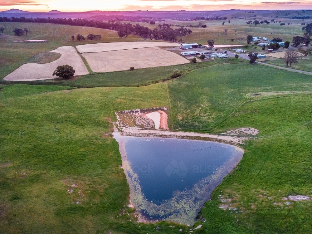 Image of Aerial view of a dam and ploughed paddocks near farm buildings ...