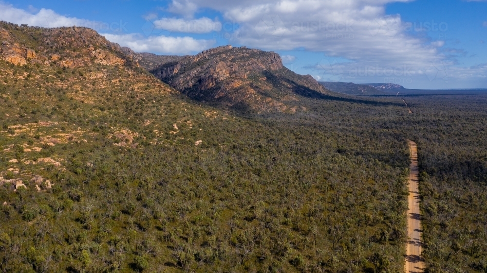 Image of Aerial view of a dirt road running through the bush below rugged mountain peaks ...