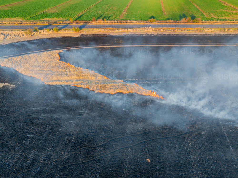 Image of Aerial view of a fire burning off stubble in a blackened ...