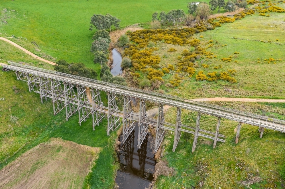 Image of Aerial view of a long wooden trestle bridge across a green ...