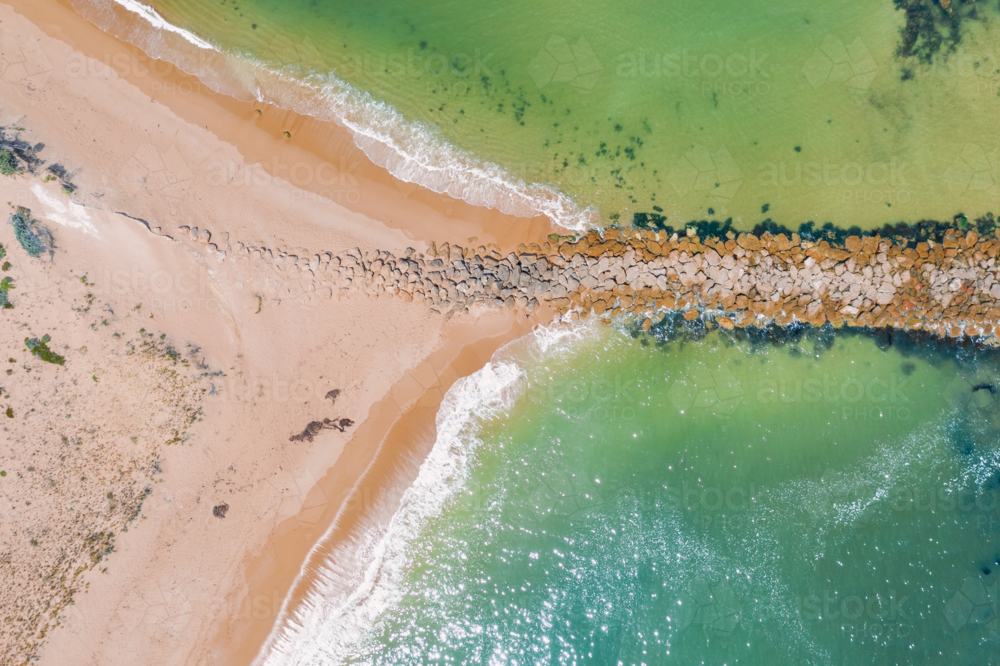 Image of Aerial view of a narrow rocky breakwater off a sandy beach ...