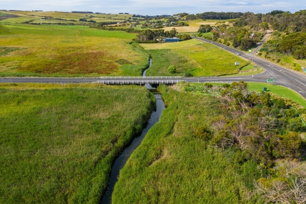 Image of Aerial view of a river flowing under a road bridge through a ...