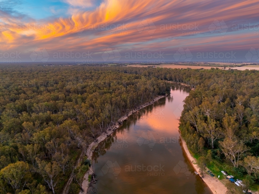 Image of Aerial view of a river lined with trees and a colourful sunset ...