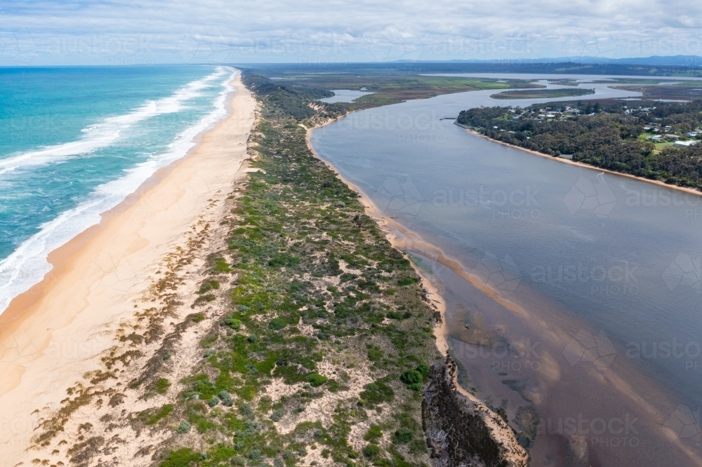 Image of Aerial view of a river running along side a sandy beach ...