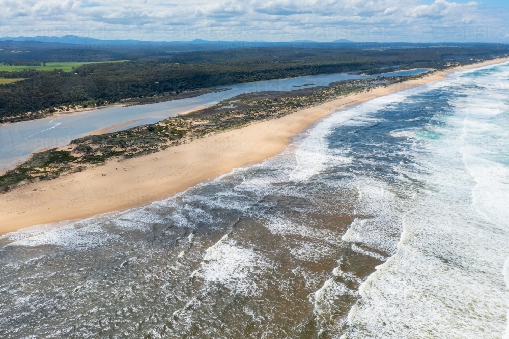 Image of Aerial view of a river running along side a sandy beach with ...