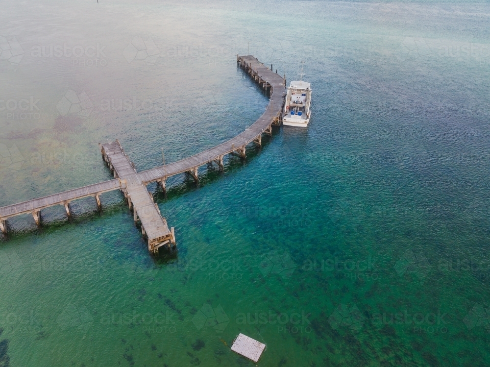 Image of Aerial view of a small boat alongside a curved wooden jetty on ...