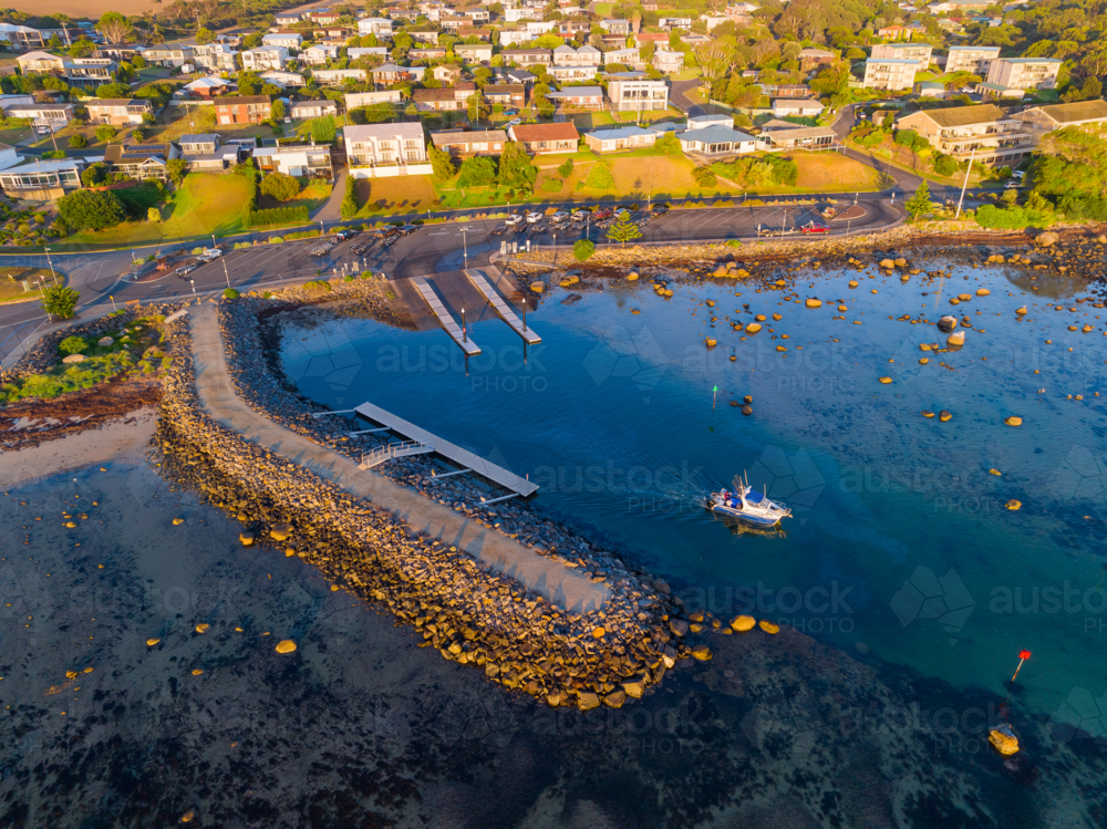 Image of Aerial view of a small boat leaving s rocky breakwater ...