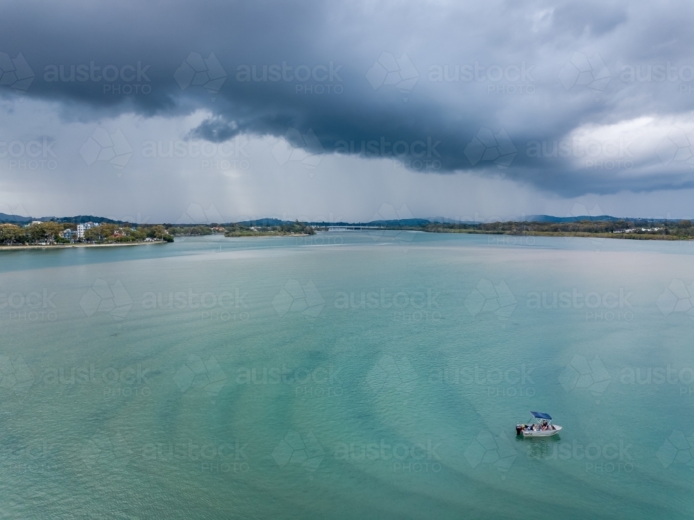 Image of Aerial view of a small boat on a river under dark storm clouds ...