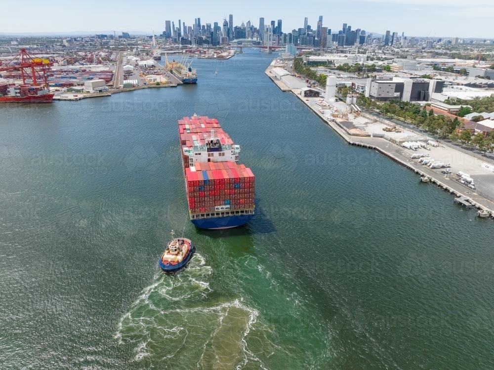 Image of Aerial view of a tugboat moving a large cargo ship up a river ...