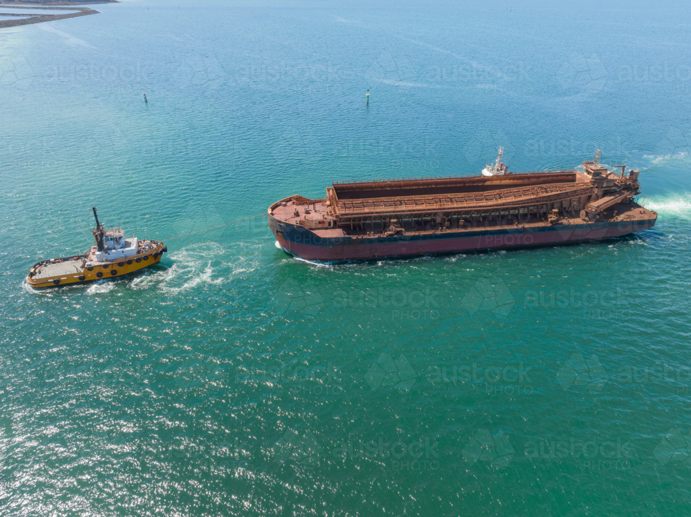 Image of Aerial view of a tugboat pulling a bulk ore ship on a blue ...