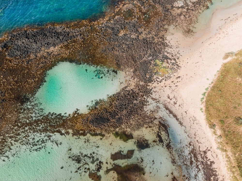 Image of Aerial view of a turquoise blue rockpool alongside a sandy ...